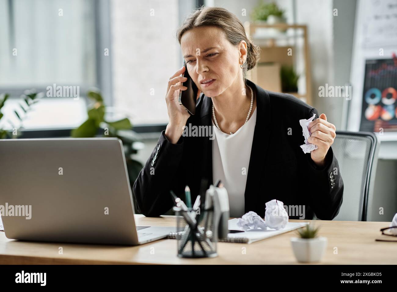 A middle-aged woman talks on the phone at her desk, showing signs of ...