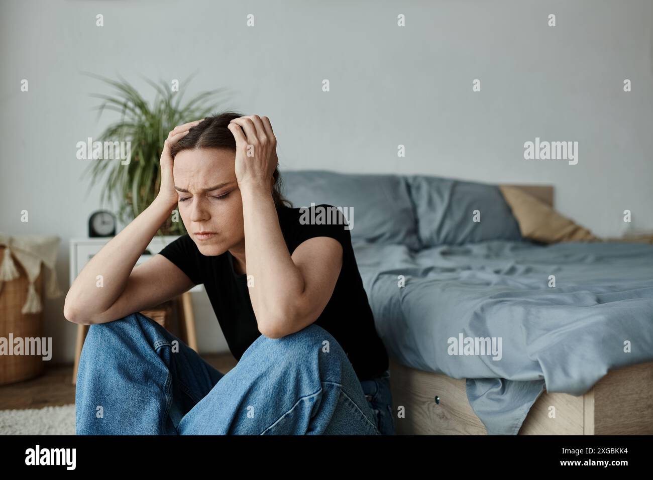Middle-aged woman in distress, sitting on floor with hands on head ...