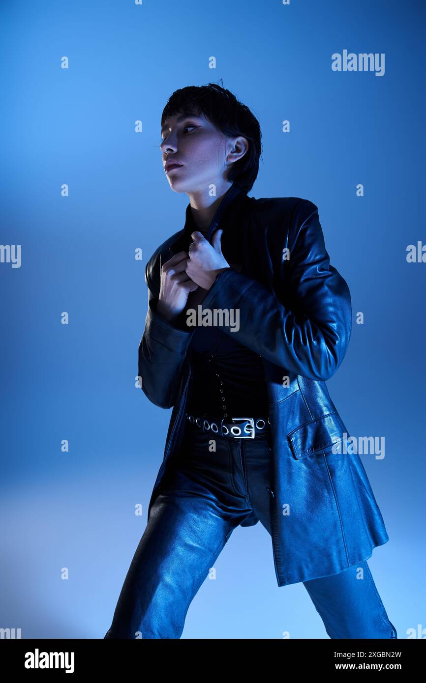 Young woman strikes a pose in leather jacket against blue backdrop ...