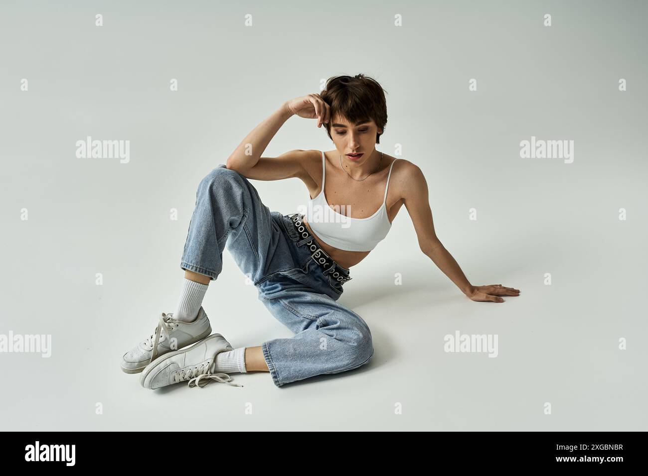 Stylish woman in white top and jeans sitting gracefully on floor Stock ...