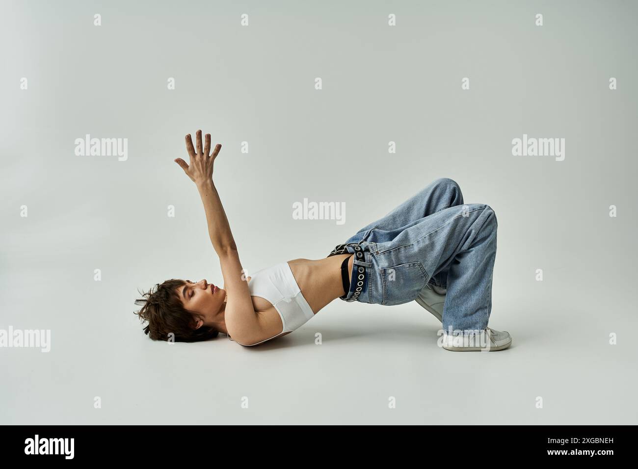 A beautiful young woman laying on her back in stylish attire on a white ...