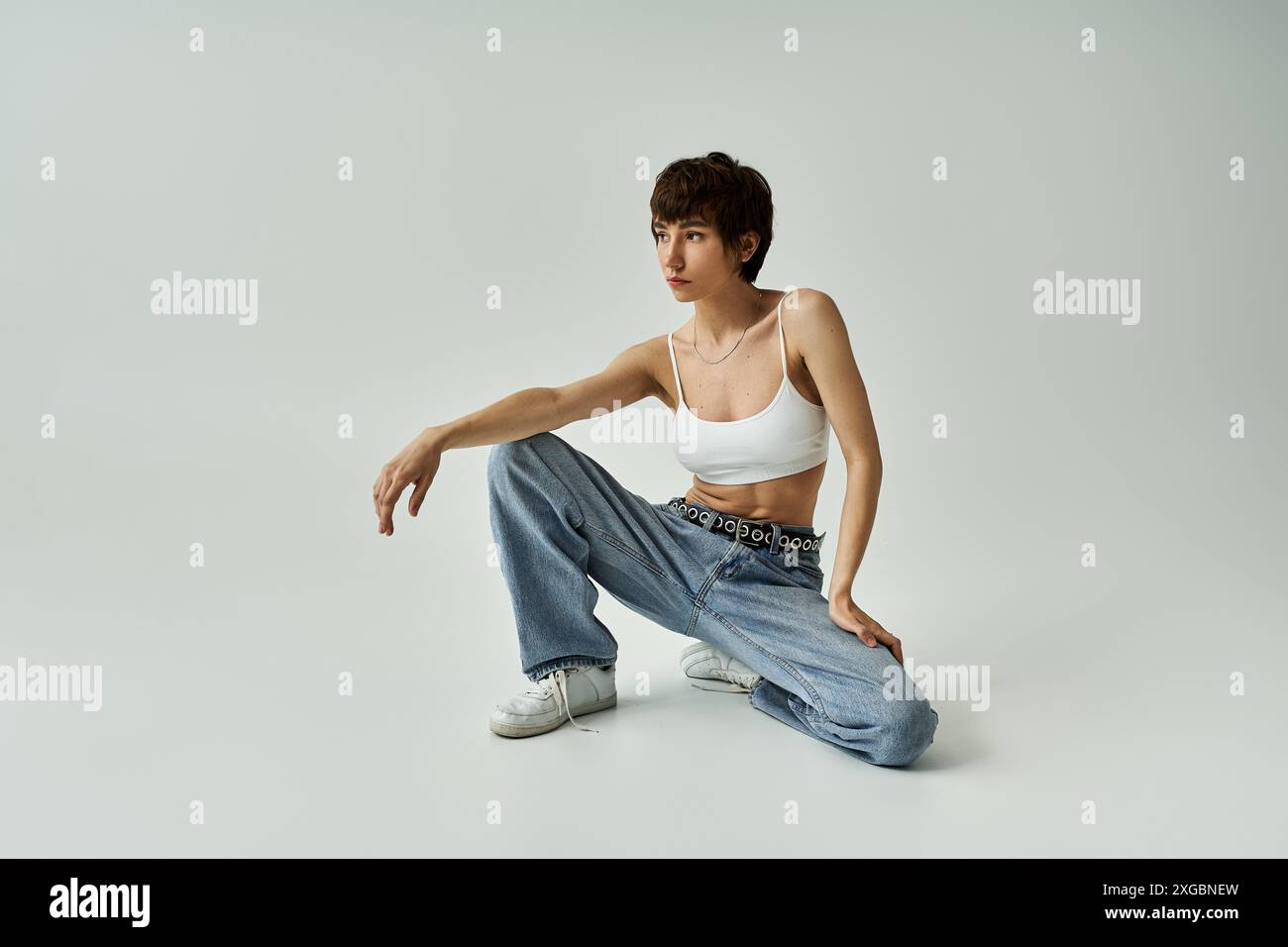 A stylish woman in white tank top and jeans poses gracefully on a white ...
