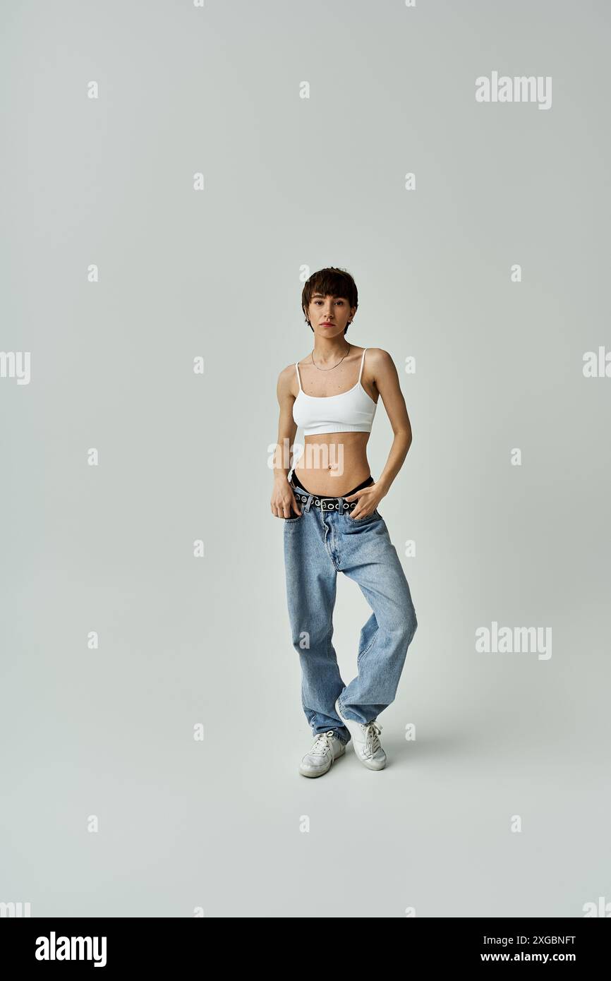 Stylish young woman poses gracefully in jeans and a white tank top ...