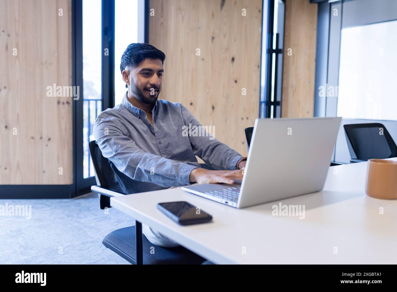 Working on laptop, man sitting at desk in modern office with smartphone ...