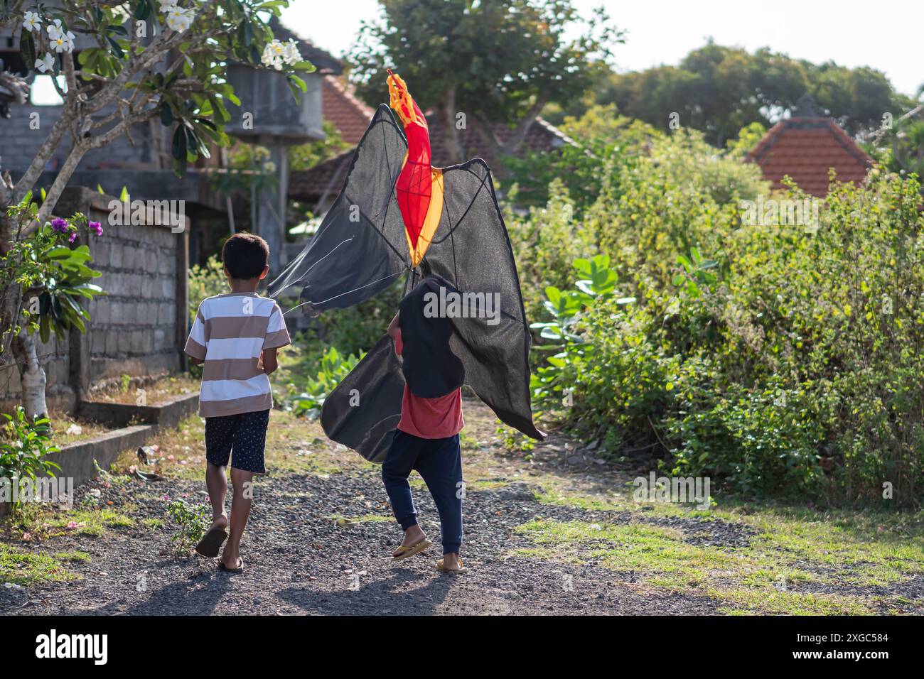 Two children walking on a path while carrying a large kite. The ...