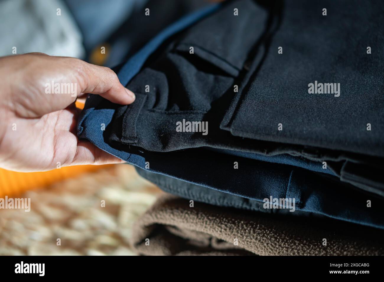A person sorting through a stack of folded clothes, focusing on dark ...