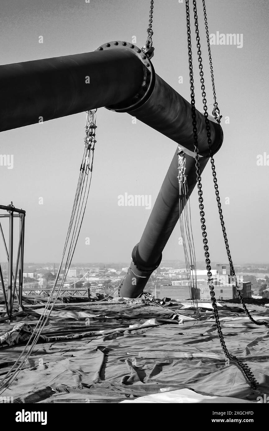 A grayscale vertical shot of a huge pipe lifted by heavy chains on a ...