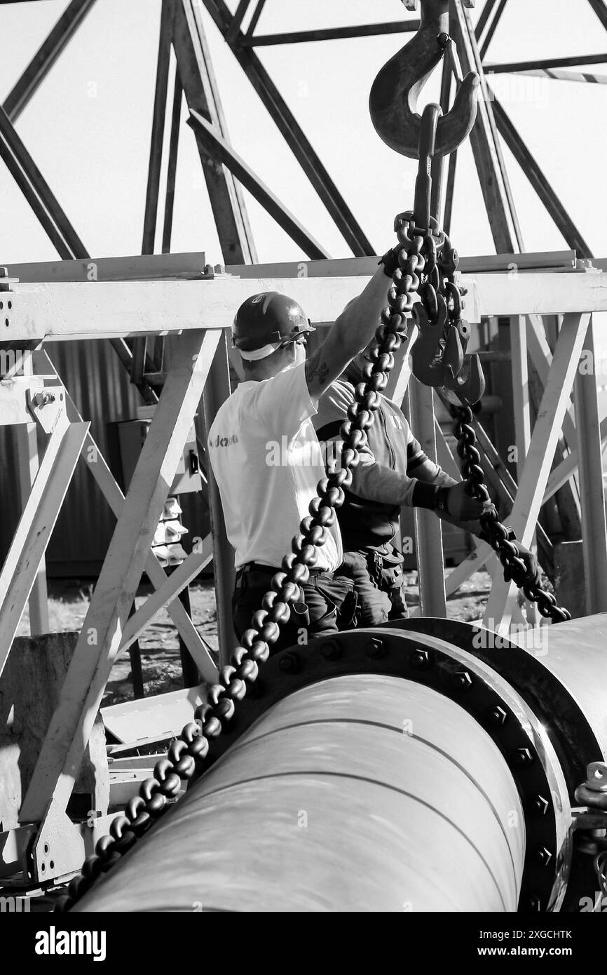 A grayscale vertical of construction workers with crane's chain to lift ...