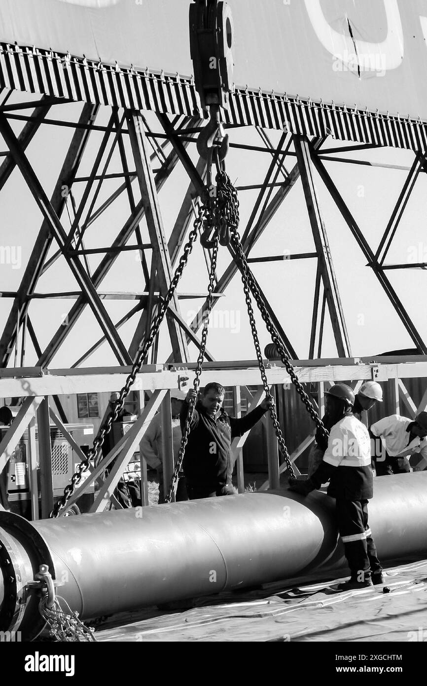 A grayscale vertical of construction workers with crane's chain to lift ...