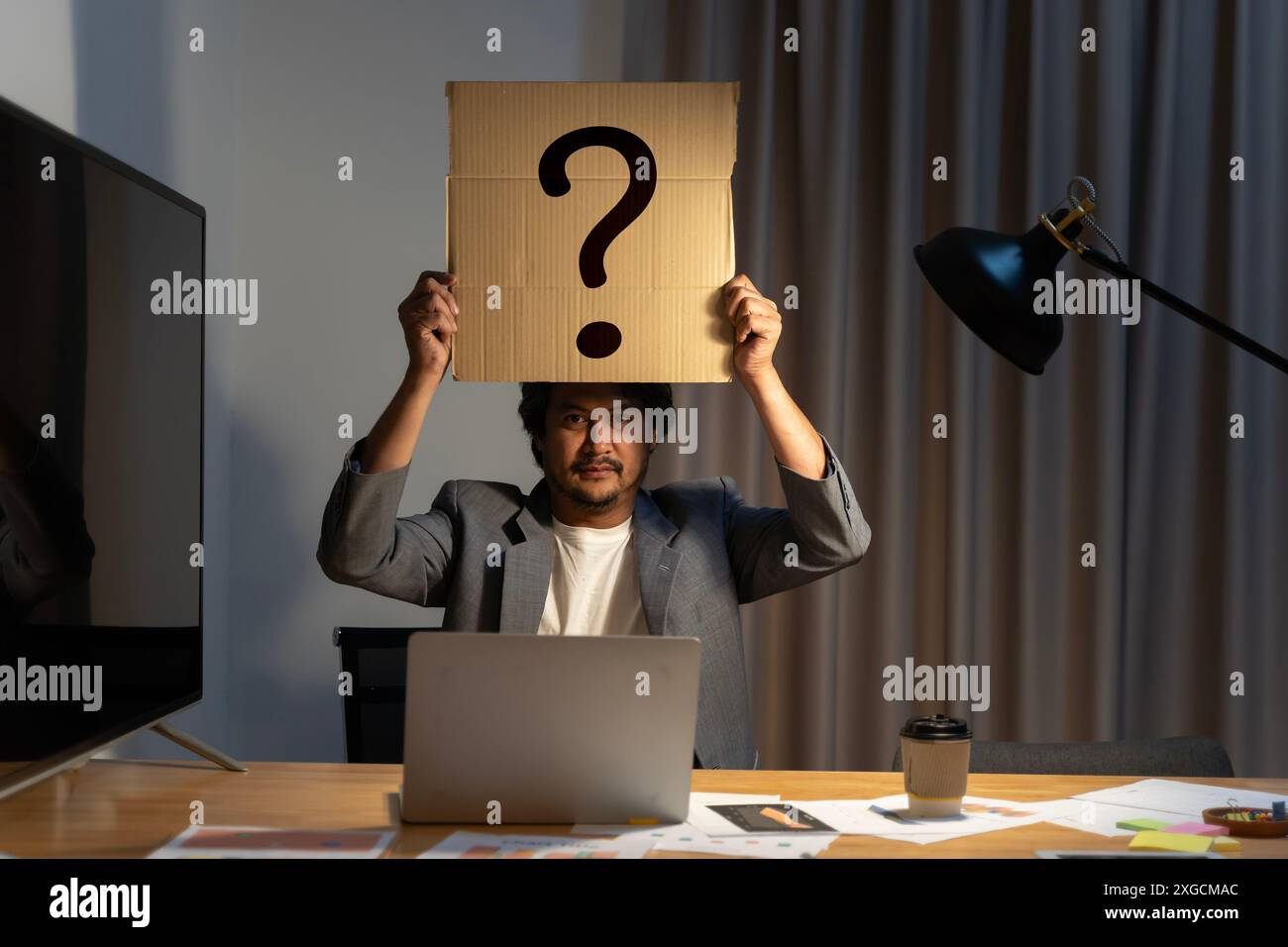 Young man with a question sign on a card covering face. Employee's ...
