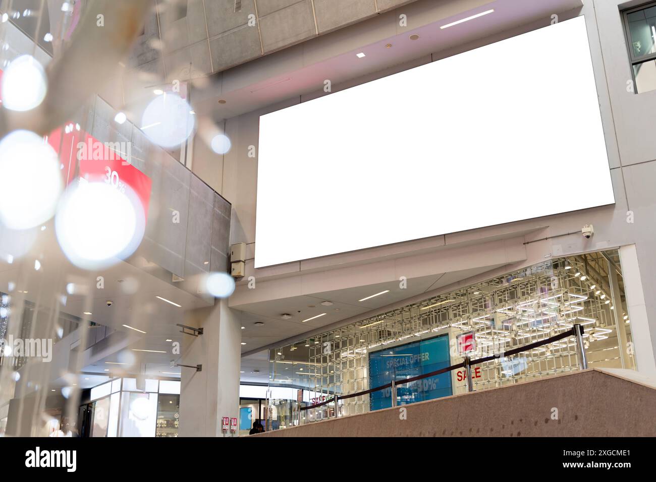 A large white billboard hangs from the ceiling of a shopping mall. The ...