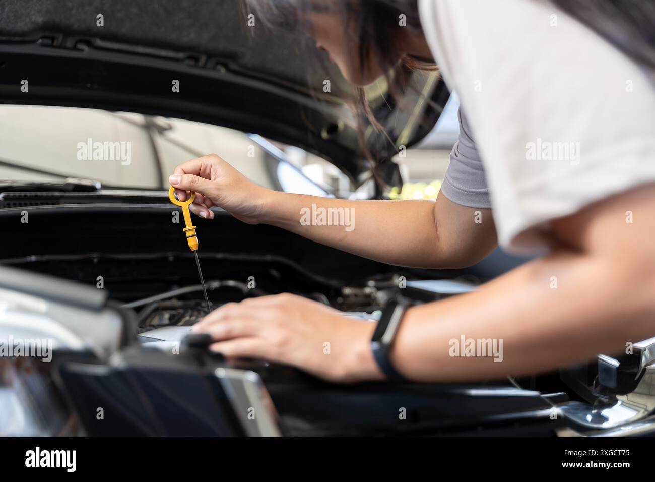 A woman pulls out the dipstick to check the oil level of her car, close-up photo of woman's hand ...