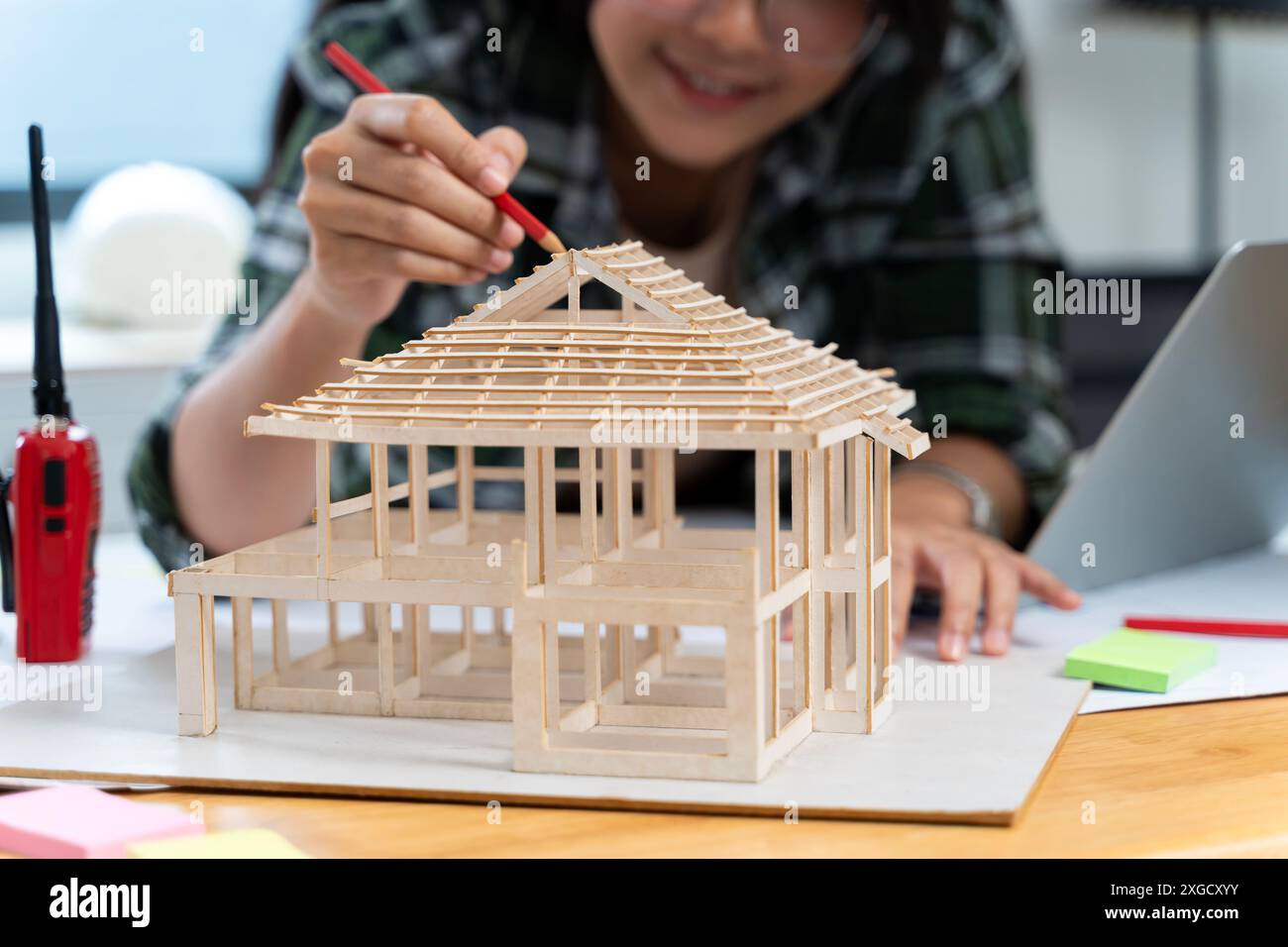Young elegant female architect with paper and pen bending over model of ...