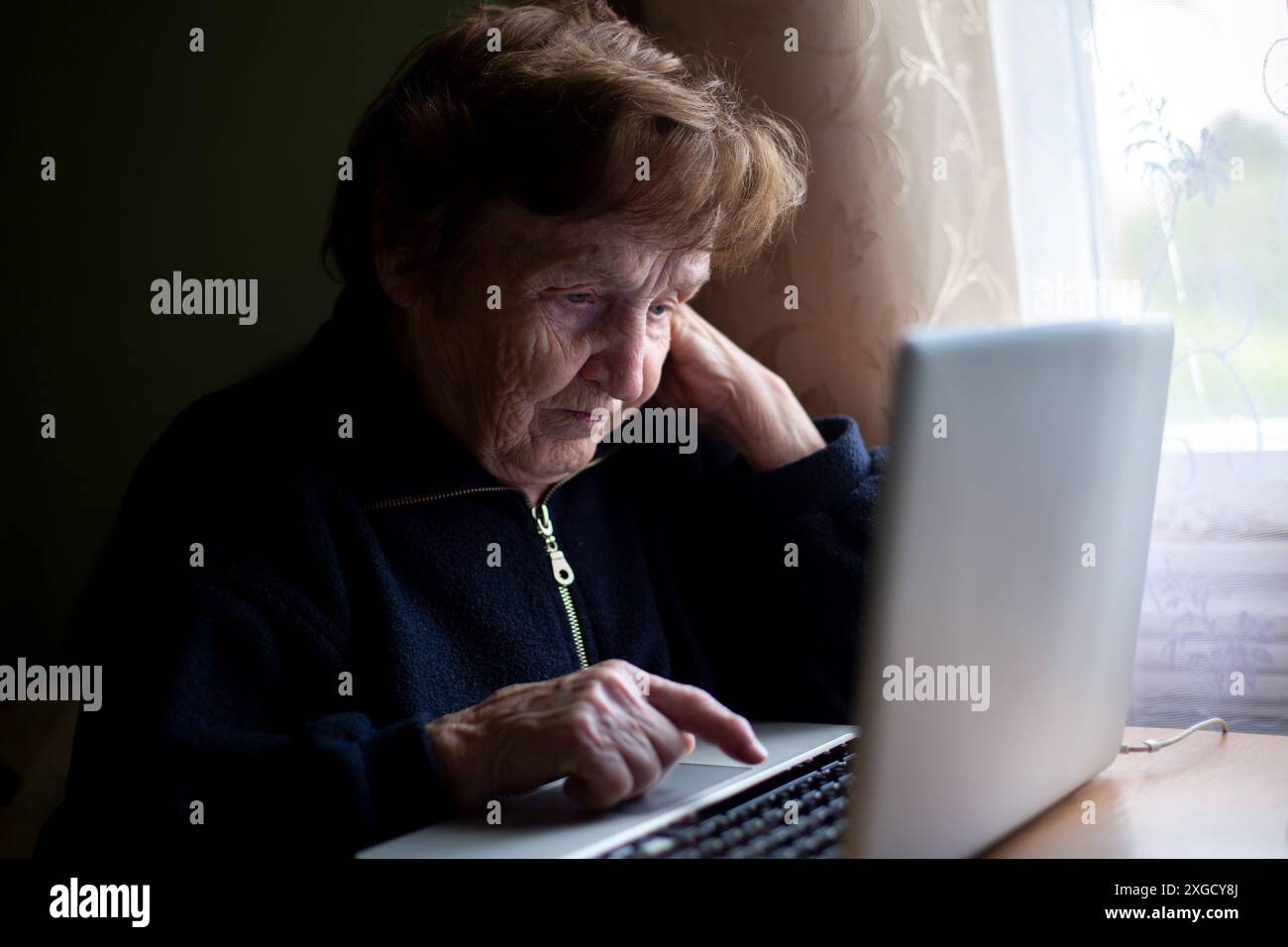 An elderly woman typing on a laptop keyboard, learning on her own at ...