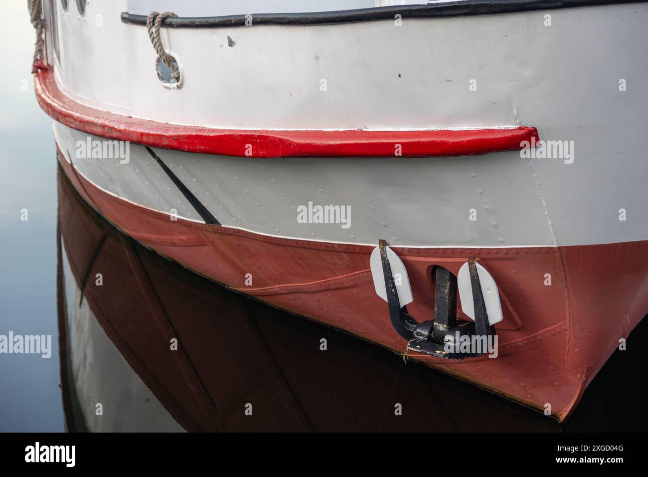 A boat with a red stripe and an anchor is docked in a harbor, its ...