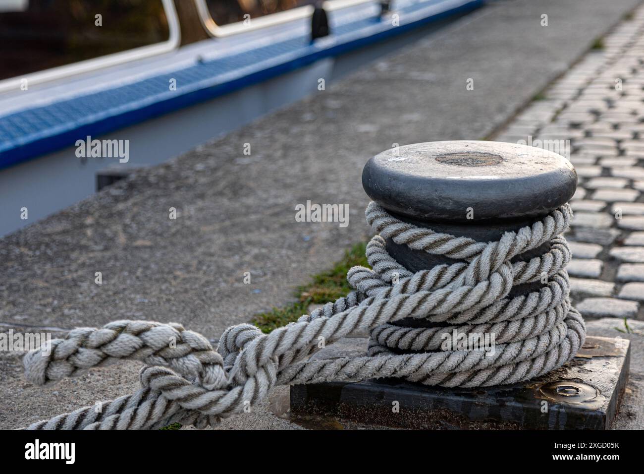 A thick white rope is wrapped around a gray metal bollard, securing a ...