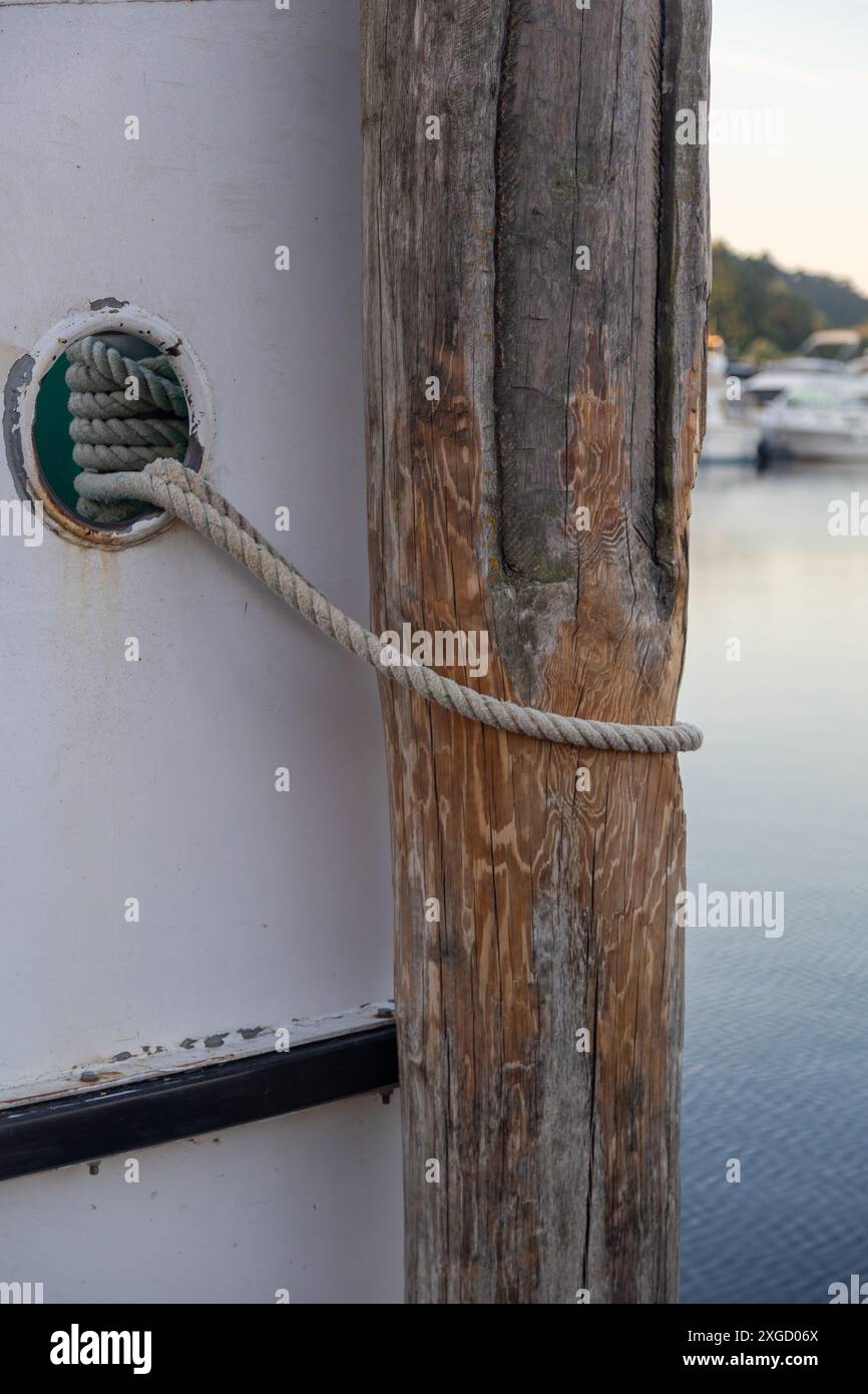 A white boat is tied to a weathered wooden dock post (dolphin) with a ...