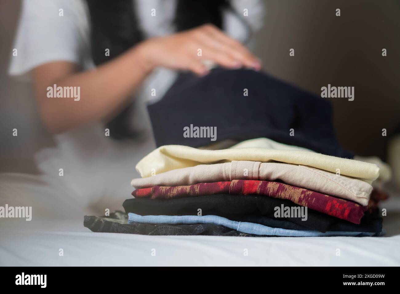 A person folding a stack of neatly folded clothes on a bed. The clothes ...