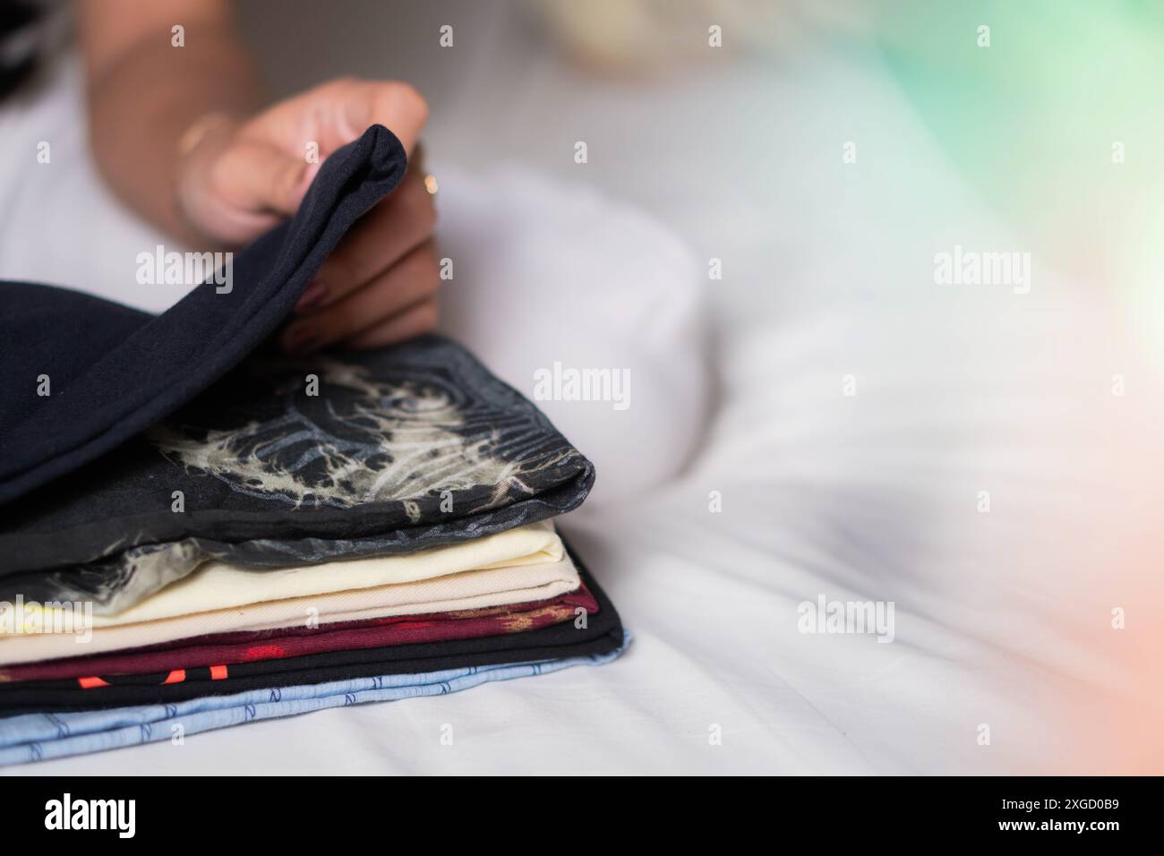 A person folding a stack of clothes on a bed, focusing on the hand and ...