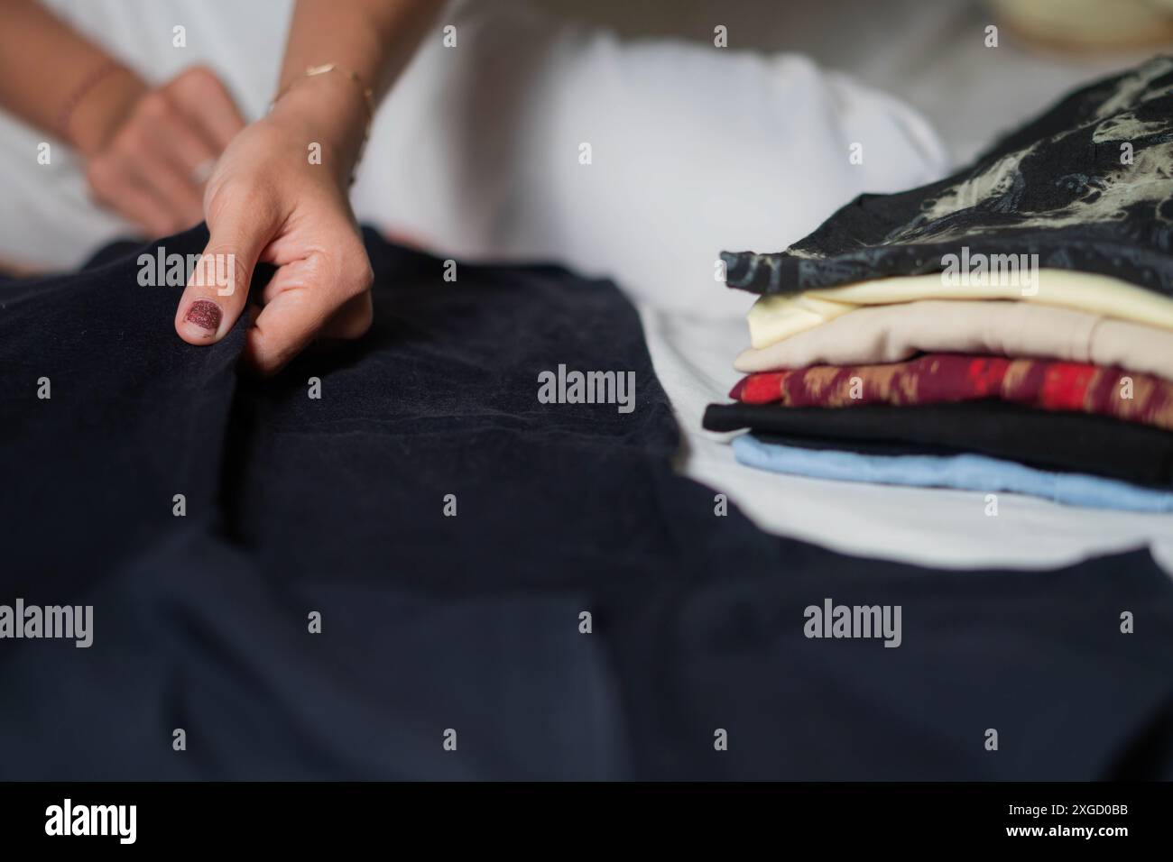 A person folding dark-colored clothes with a stack of folded clothes ...
