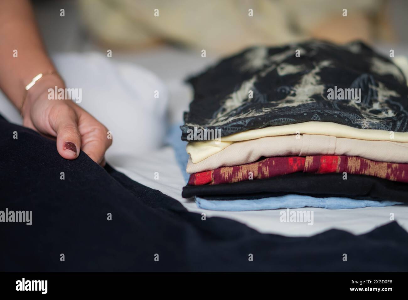 A person folding a stack of neatly folded clothes on a bed. The clothes ...