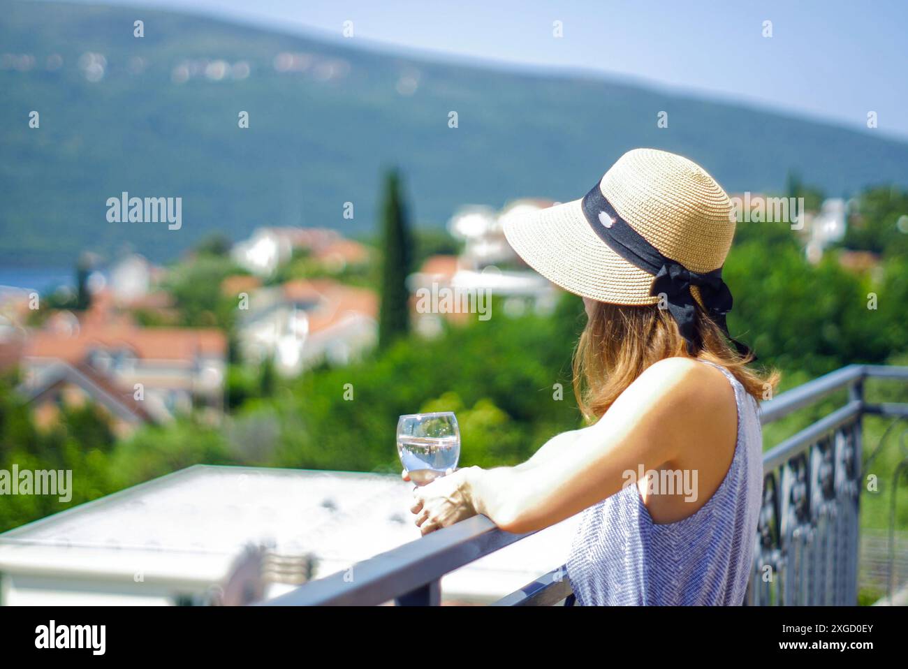 A young woman in a hat stands with a glass, leaning her elbows on the ...
