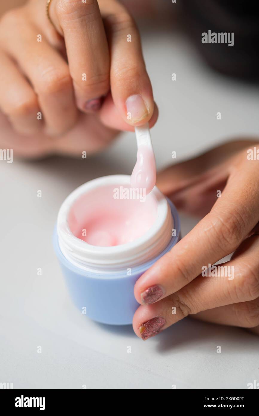 Close-up of hands using a spatula to scoop pink cream from a blue jar ...
