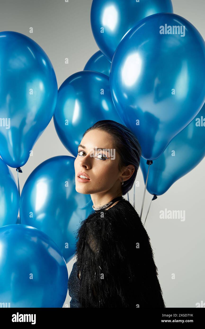 Young woman with dyed hair stands in front of a group of blue balloons ...