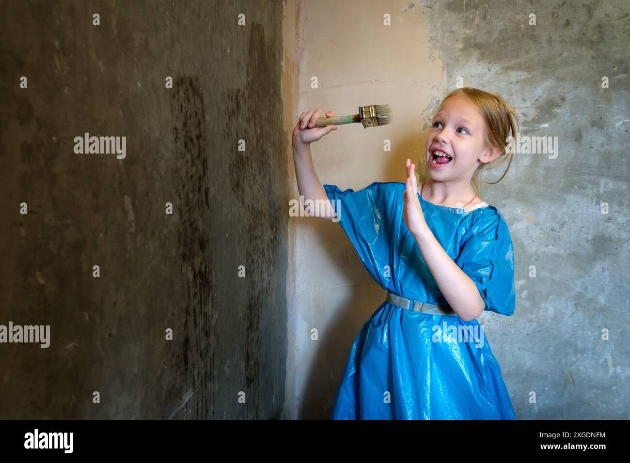 9-year-old girl in blue workwear priming a cement wall. Renovation ...