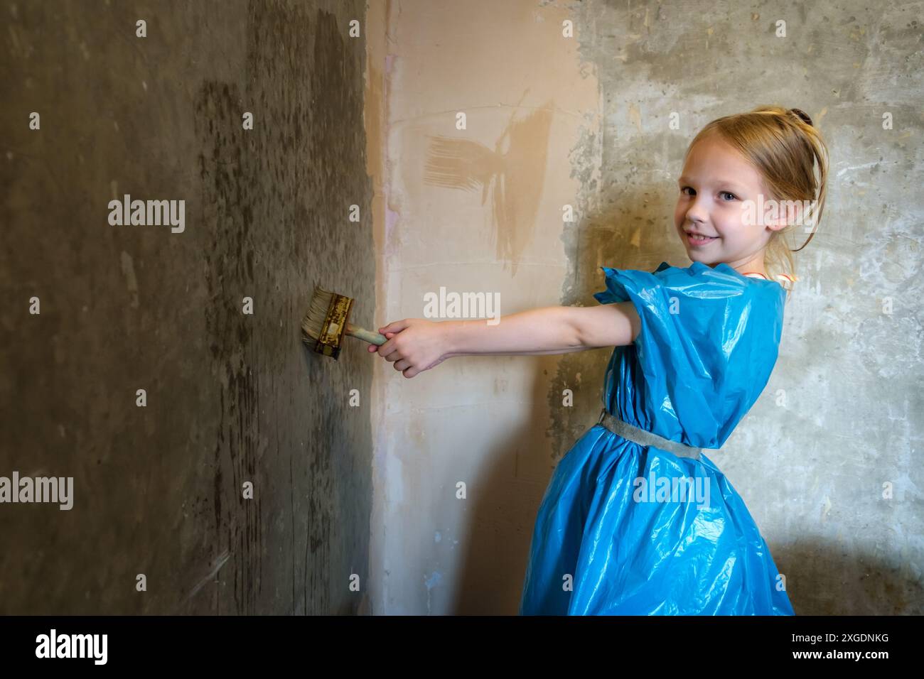 9-year-old girl in blue workwear priming a cement wall. Renovation ...