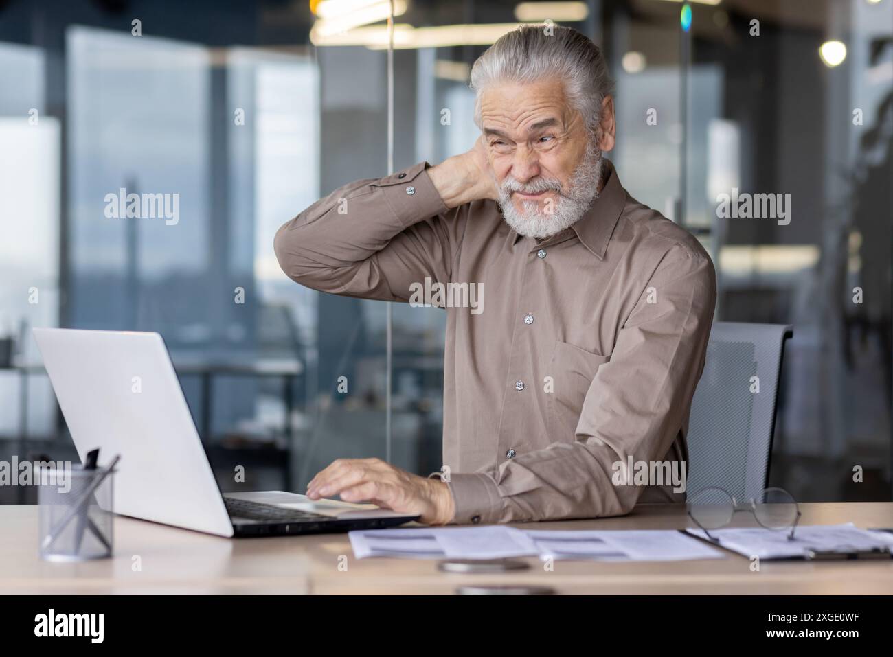 Elderly man feeling discomfort and neck pain while using a laptop at a ...