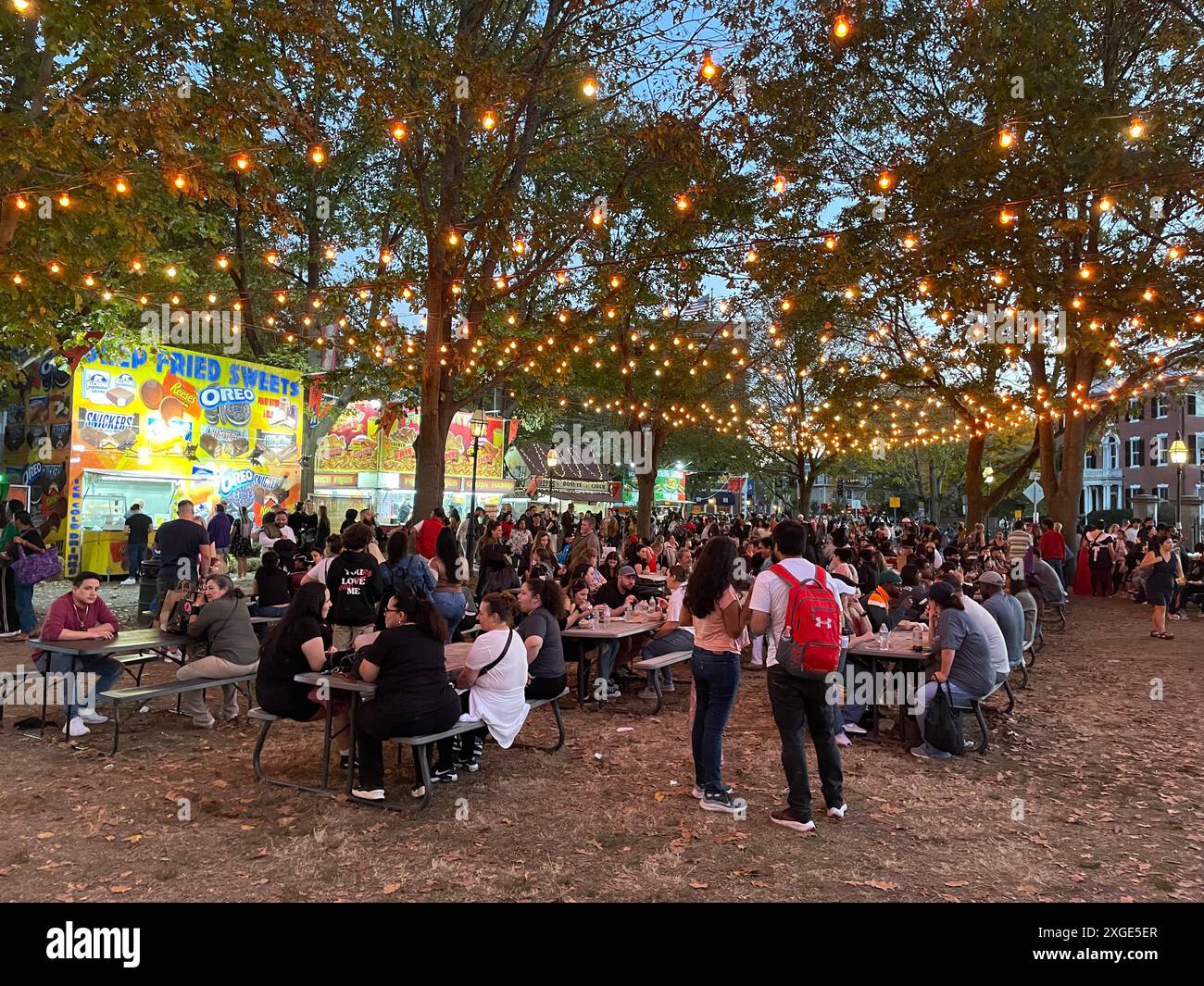 People enjoy eating their food truck dinner at night under a string of ...