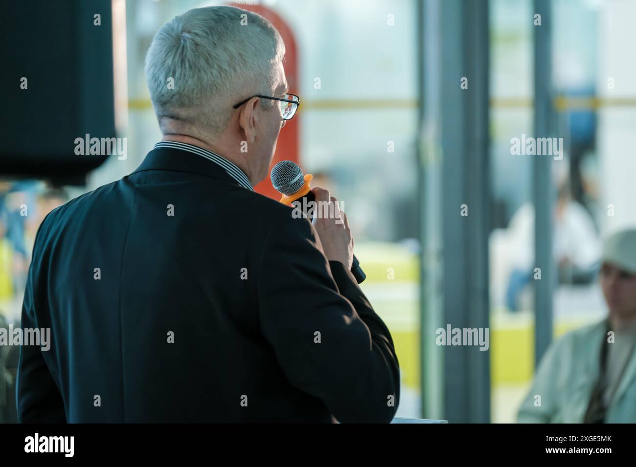 Back view of an elderly businessman speaking into a microphone at a ...