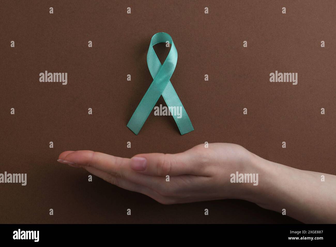 Woman with turquoise awareness ribbon on brown background, top view ...