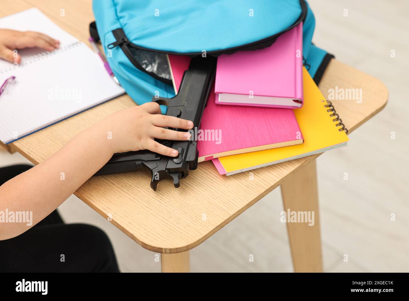 Child taking gun out of backpack at desk in classroom, closeup. School ...