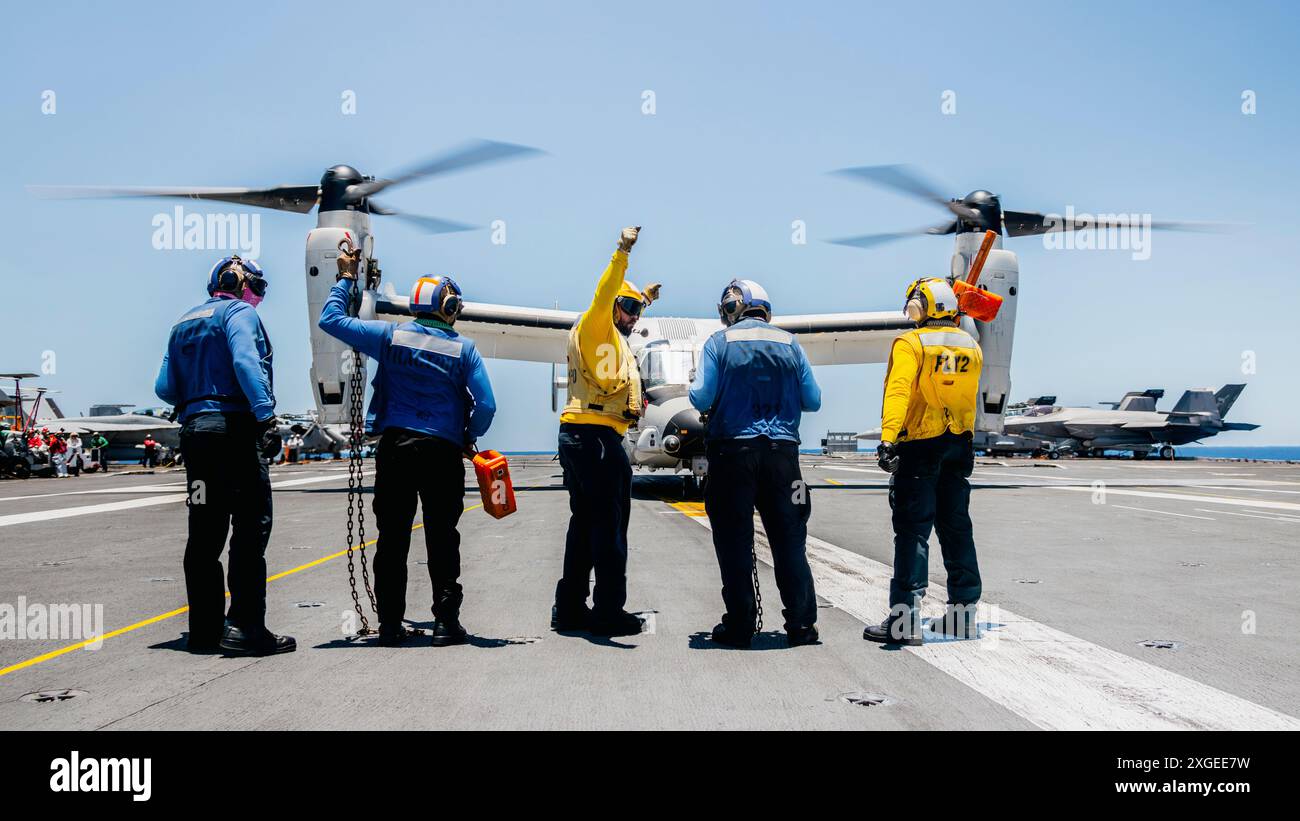 Sailors show chocks and chains to a CMV-22B Osprey on the flight deck ...