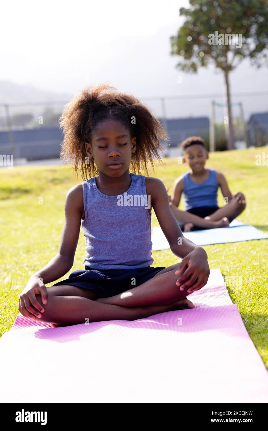 Happy african american schoolchildren doing yoga and meditating on ...