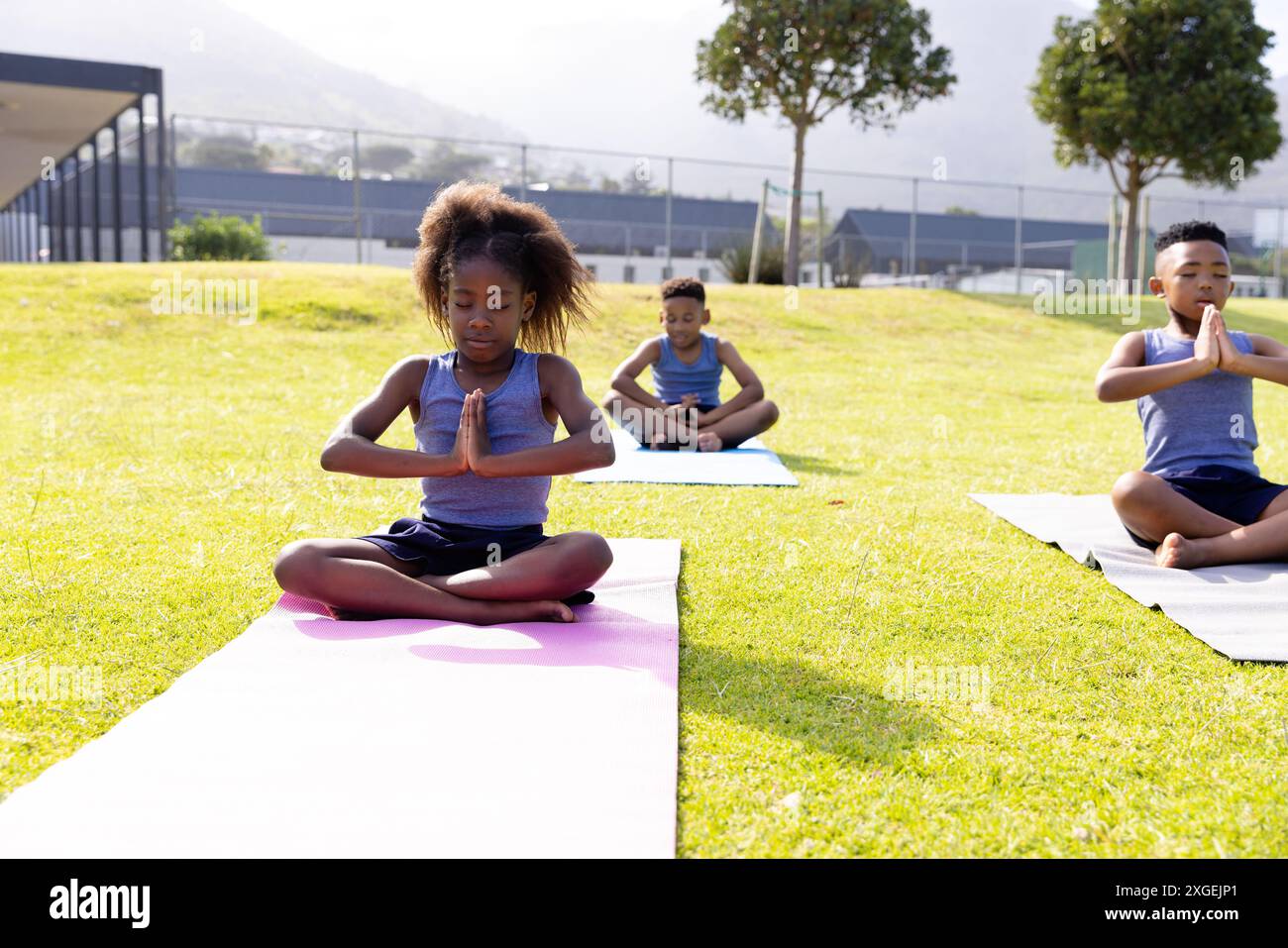 Happy african american schoolchildren doing yoga and meditating on ...