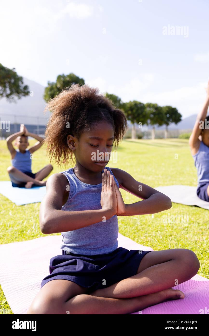 Happy african american schoolchildren doing yoga and meditating on ...