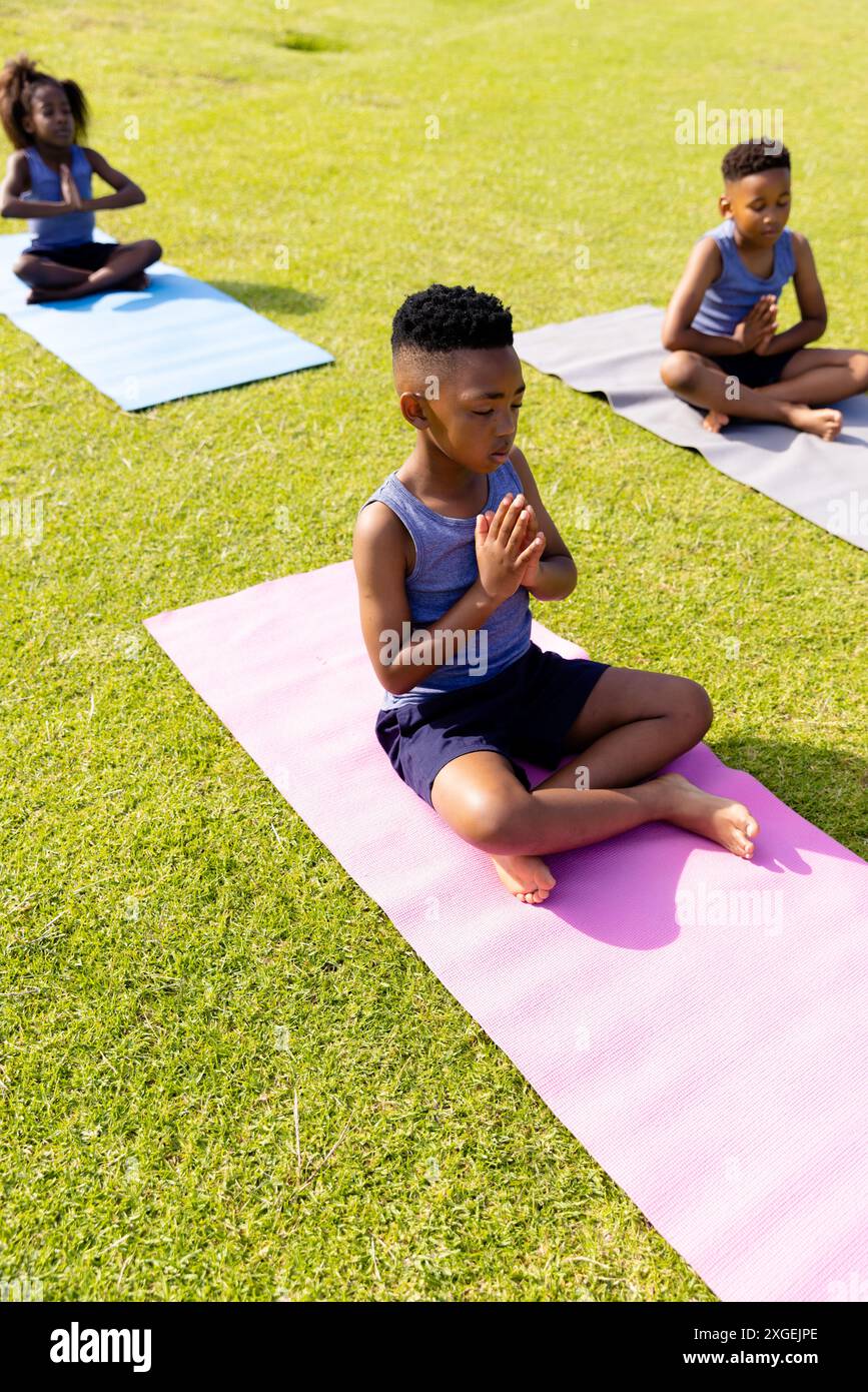 Happy african american schoolchildren doing yoga and meditating on ...