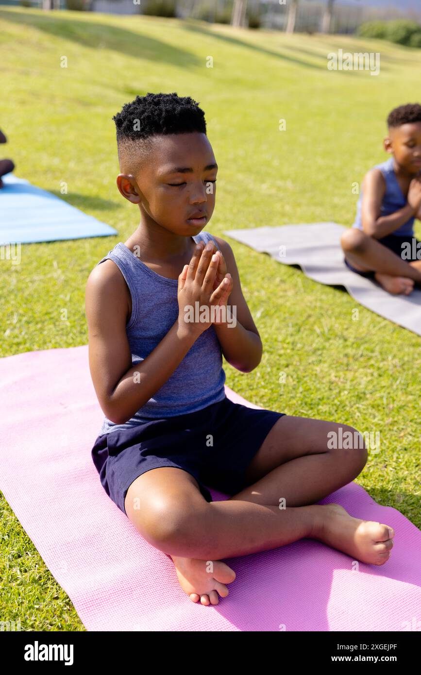 Happy african american schoolchildren doing yoga and meditating on ...