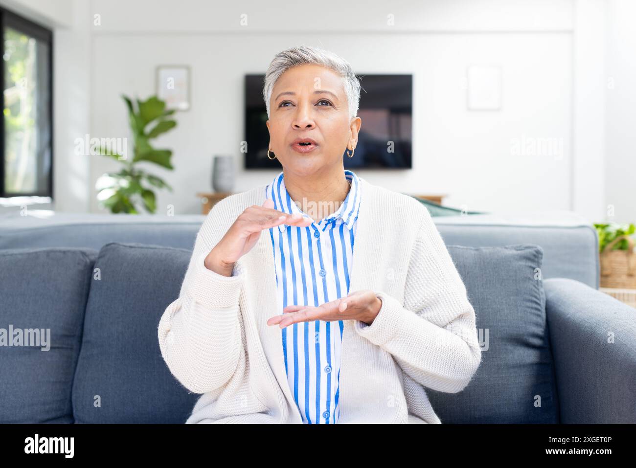 Senior woman sitting on couch, using sign language for communication ...