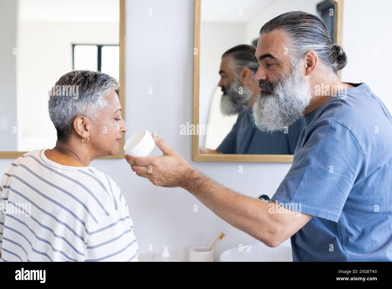 Applying face cream, senior man helping woman in bathroom, morning ...