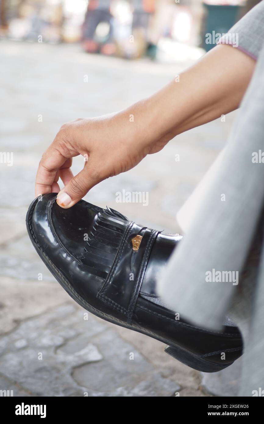 In an outdoor setting, someone adjusts a chic black leather dress shoe ...