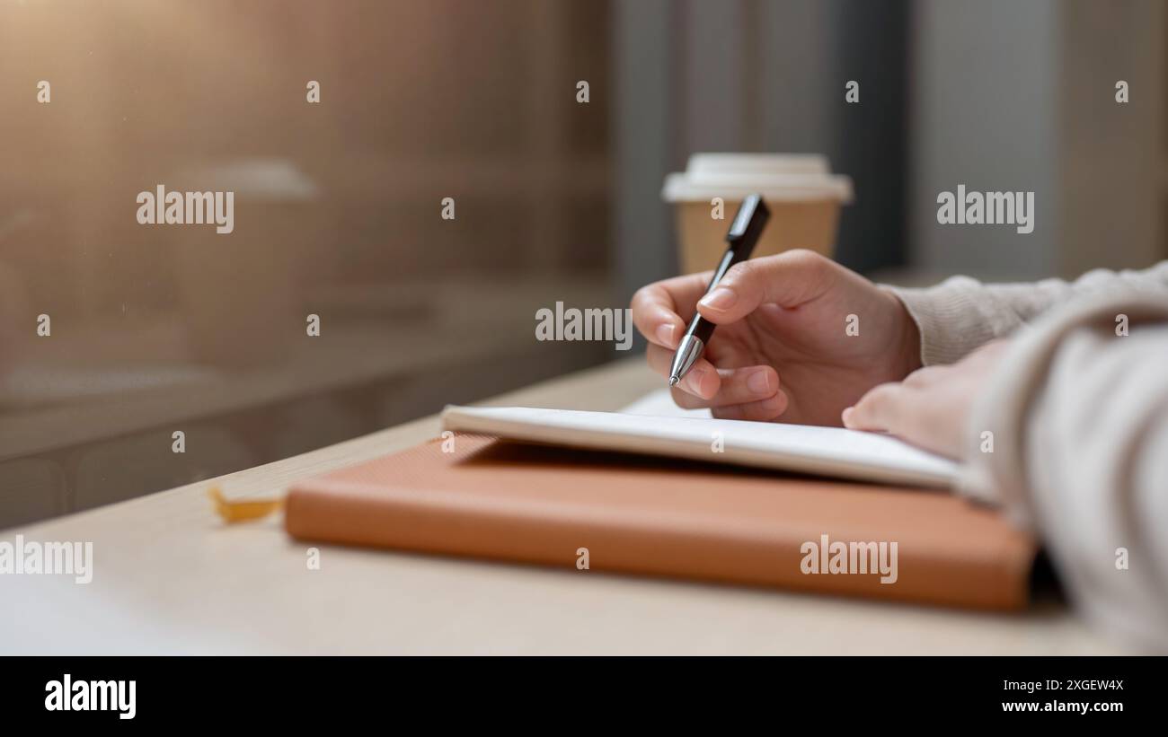 A close-up image of a woman holding a pen and writing in a notebook at ...