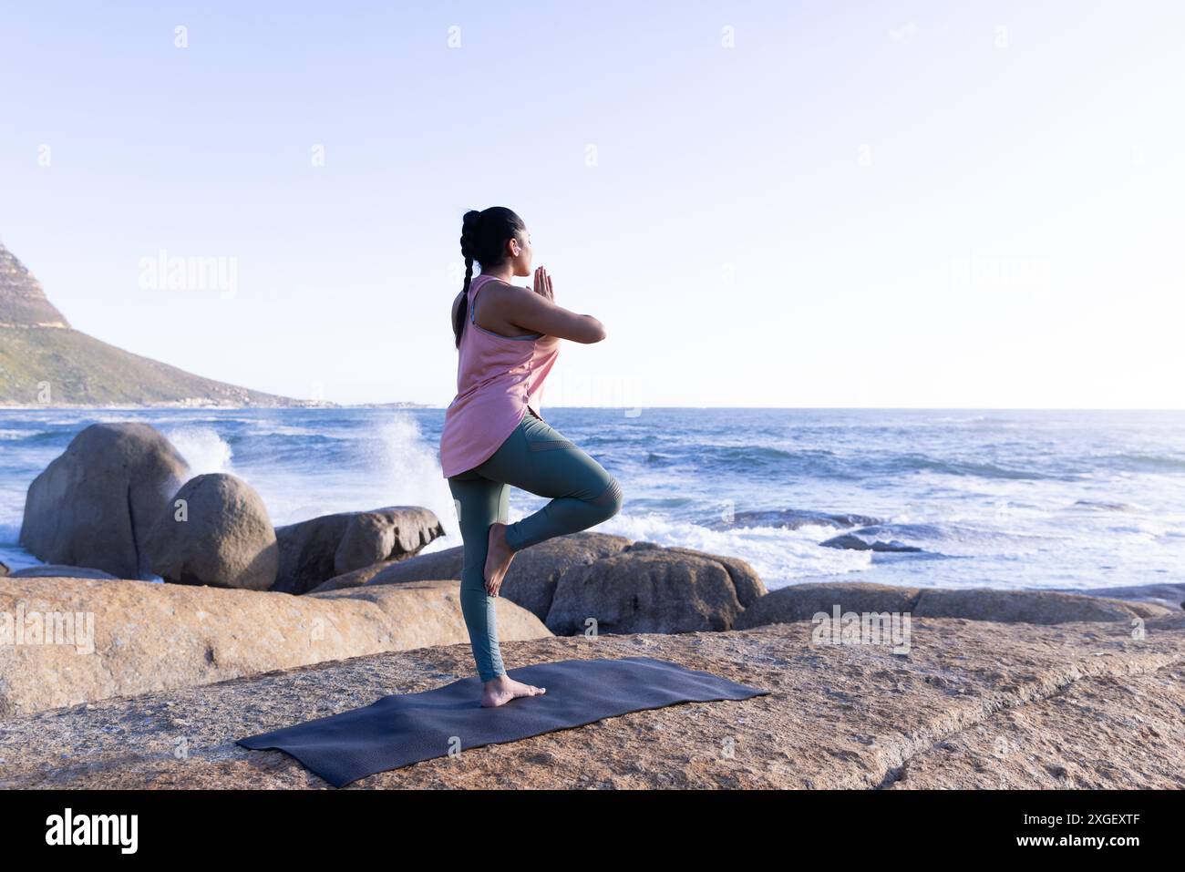 Practicing yoga, woman balancing in tree pose on yoga mat by ocean ...