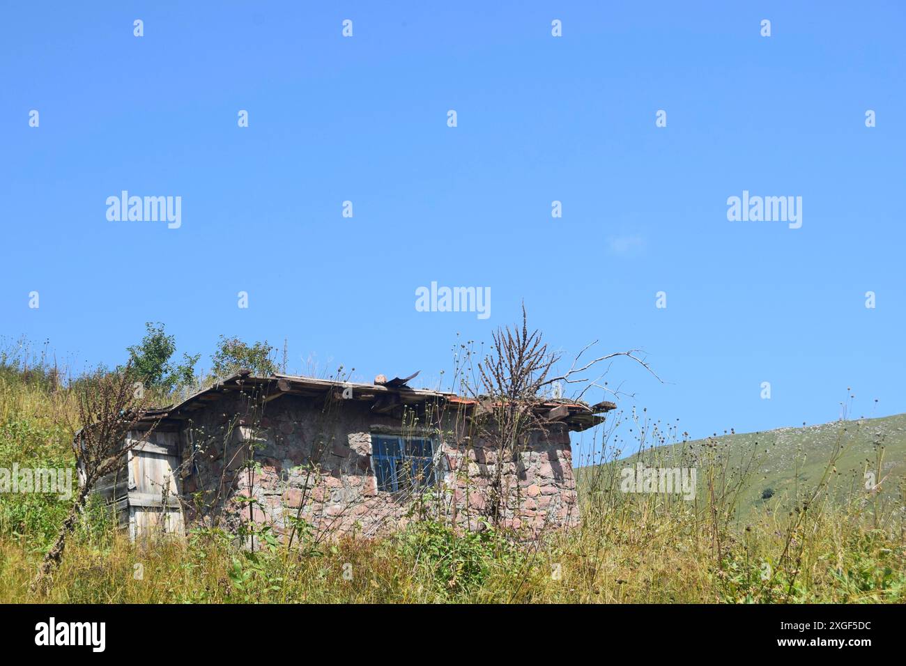 A rustic stone house on a grassy hillside under a clear blue sky Stock ...