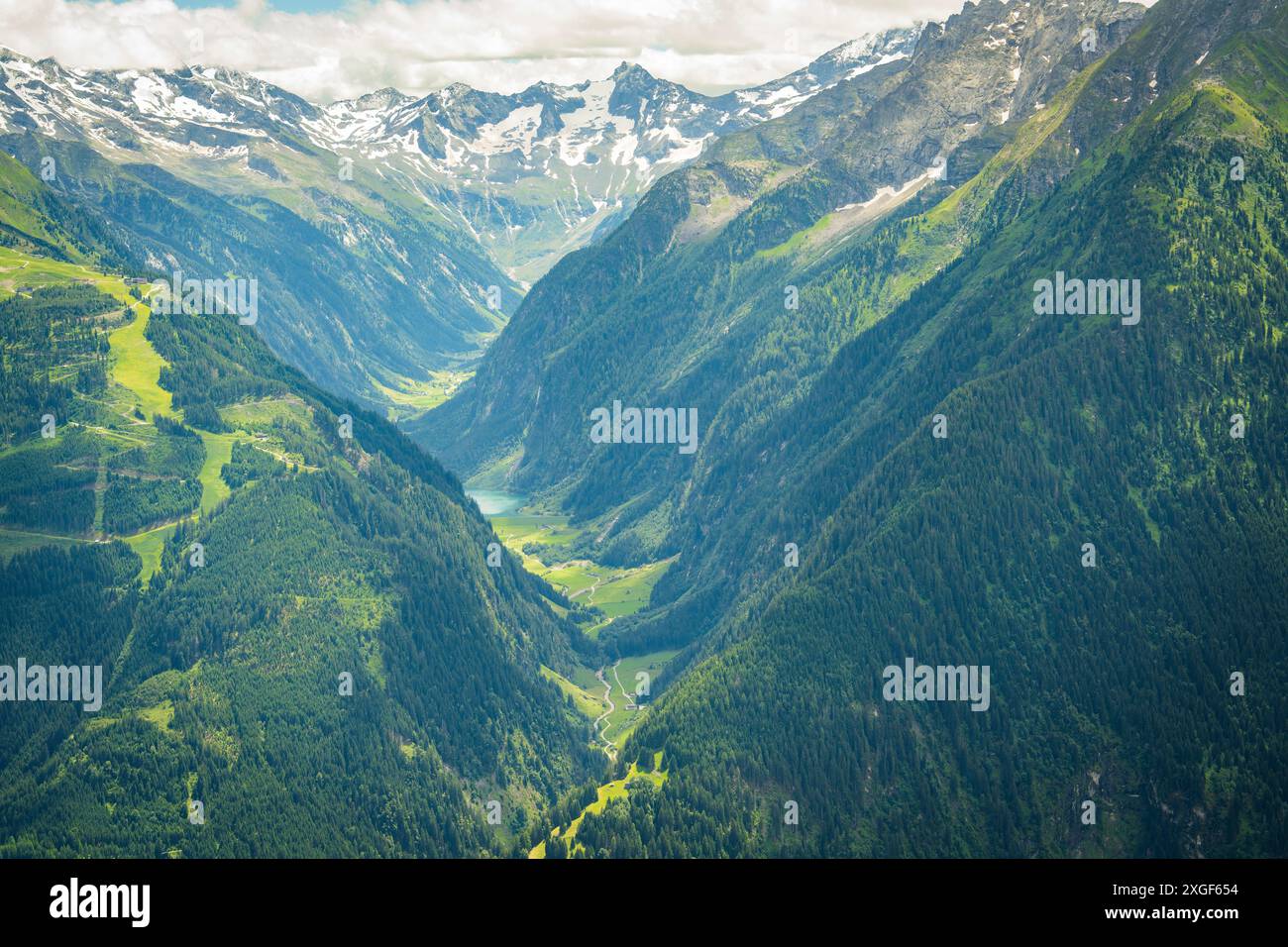 Wide valley between snow-covered mountains with green forests and ...