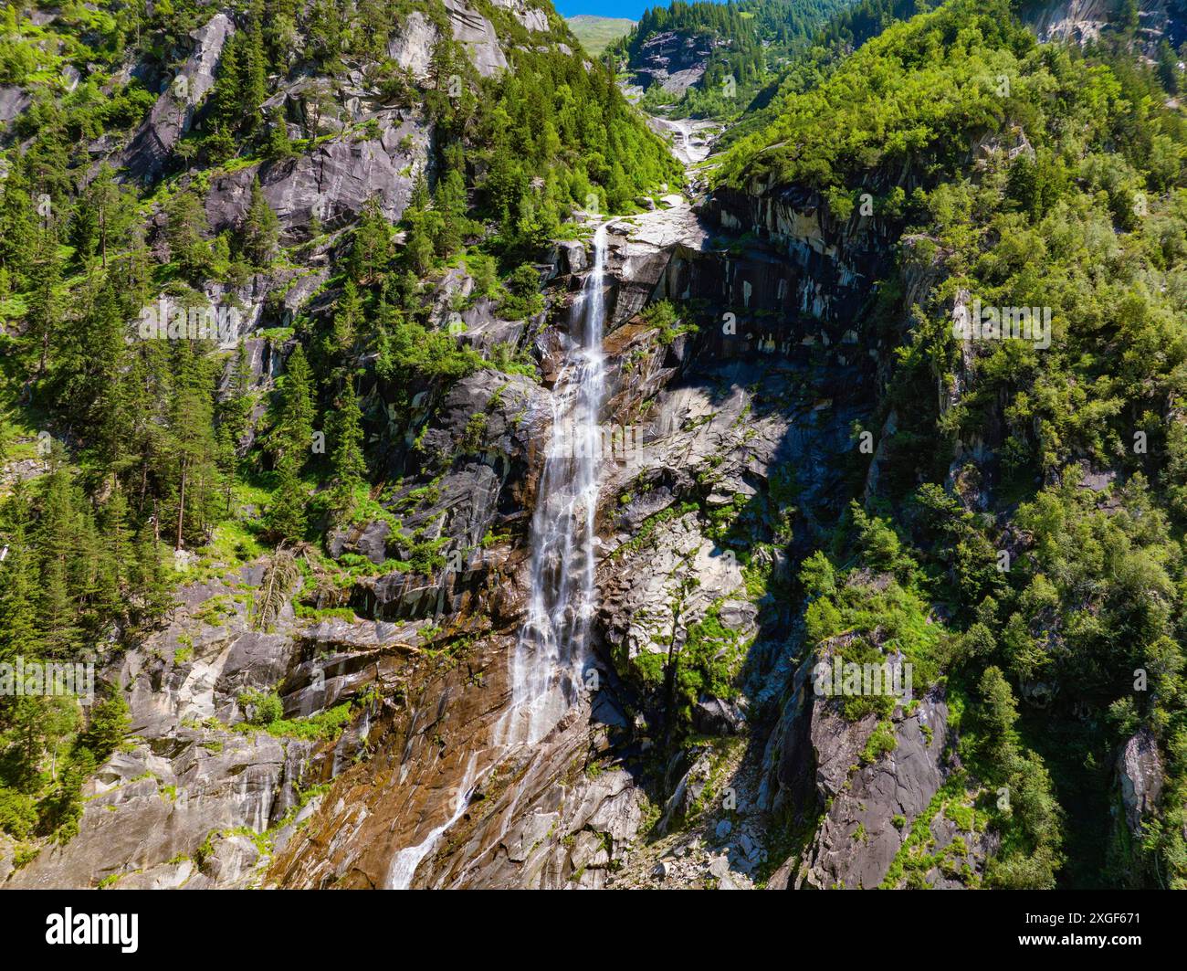 A high waterfall cascading down between rocky cliffs and dense forest ...