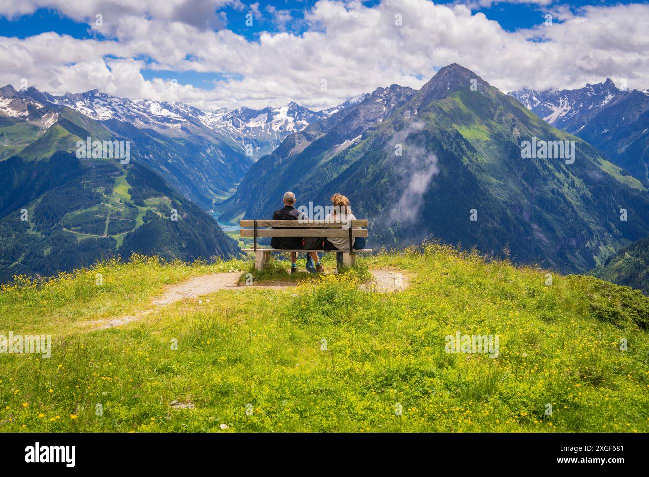 Two people sit on a bench and look out over a valley with majestic ...